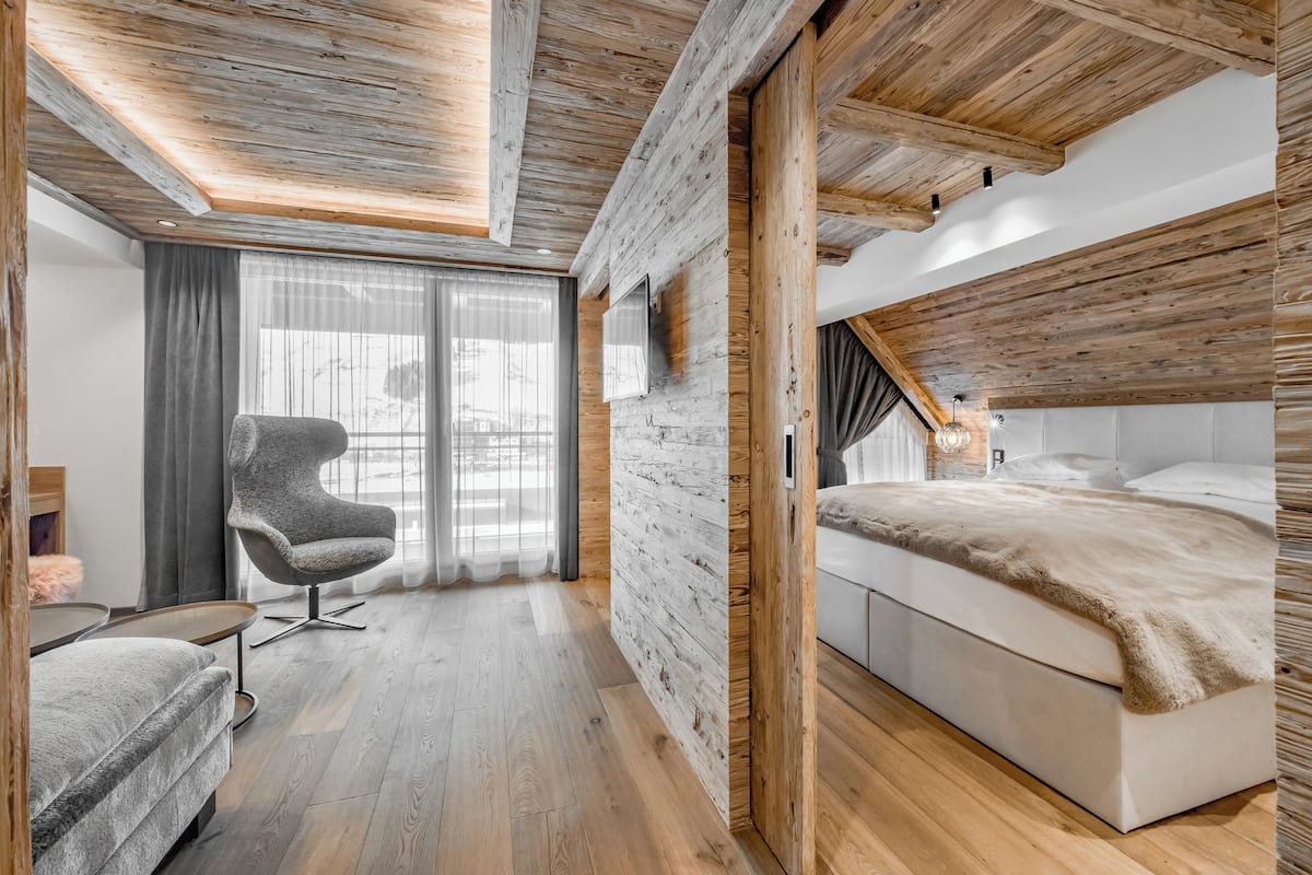 Um quarto moderno com teto de madeira, uma cama grande, uma cadeira e uma janela com cortinas.