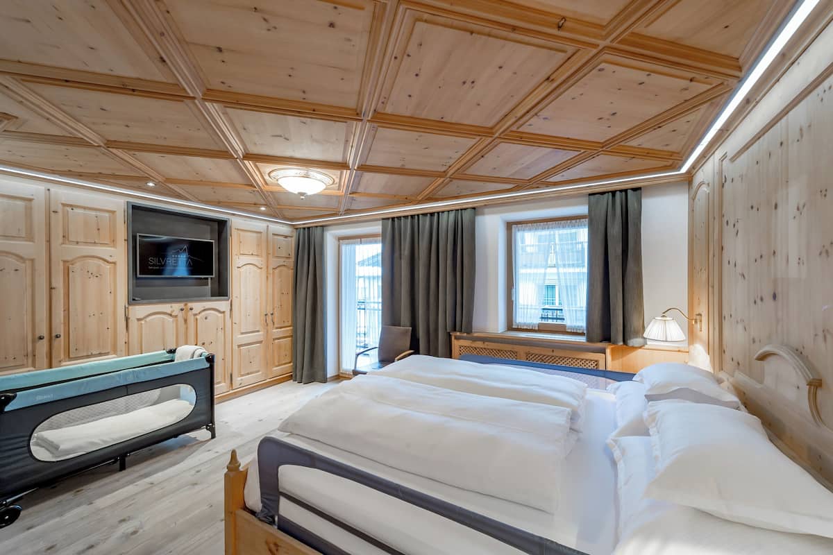 Quarto de hotel com uma cama grande, televisão, painéis de madeira e janela com cortinas.