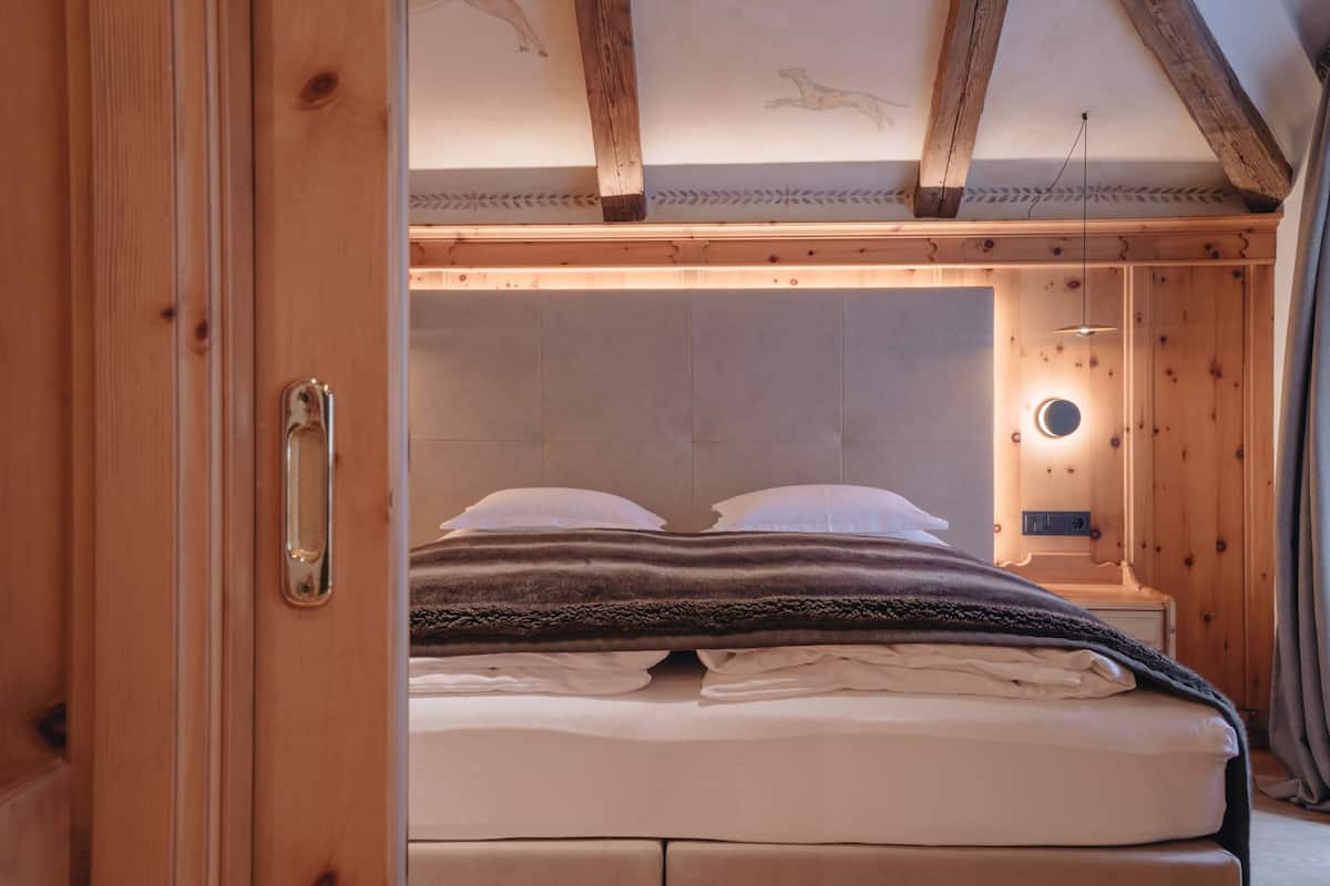 Quarto com estrutura de madeira, uma cama, um criado-mudo e um candeeiro fixo na parede.