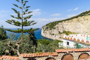 Um edifício costeiro com fachada de pedra, telhas de barro e vista para o mar.