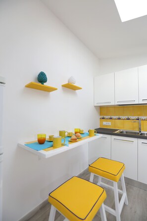 Uma cozinha com armários brancos, bancada amarela e dois bancos amarelos.