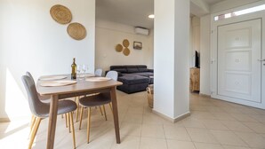 Uma sala de jantar com mesa e cadeiras de madeira, um sofá cinza escuro e uma porta branca.