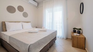 Quarto de hotel com uma cama, uma mesinha de cabeceira com uma planta e uma janela com cortinas.