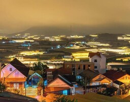 Uma aldeia rural ao entardecer, com casas e campos iluminados.