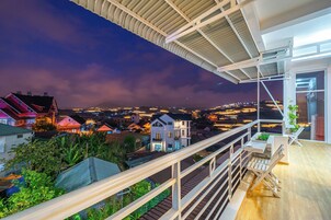 Uma varanda com vista para uma cidade à noite, um corrimão e uma mesa com cadeiras.
