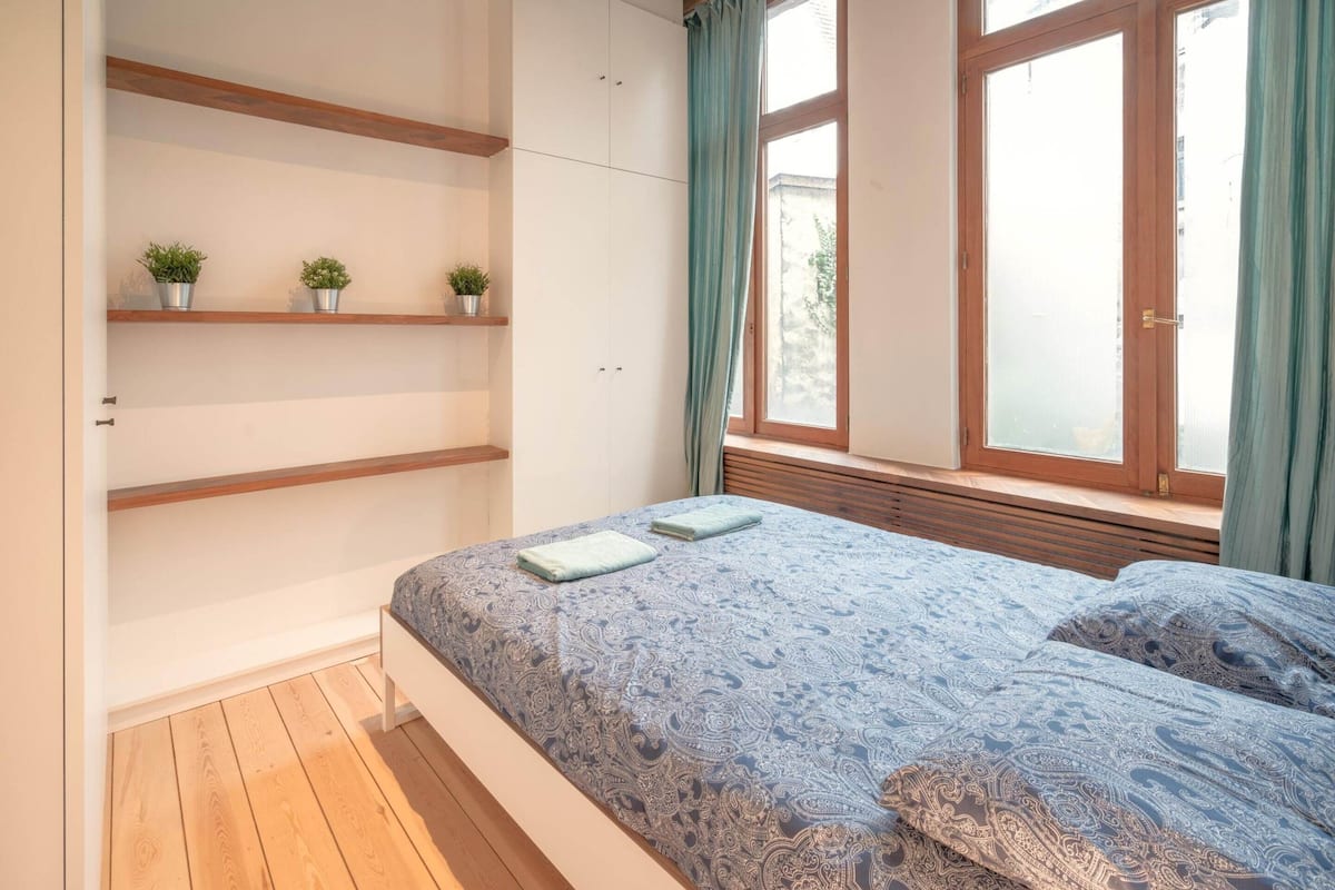 Quarto com cama, estantes embutidas e janela com cortinas.