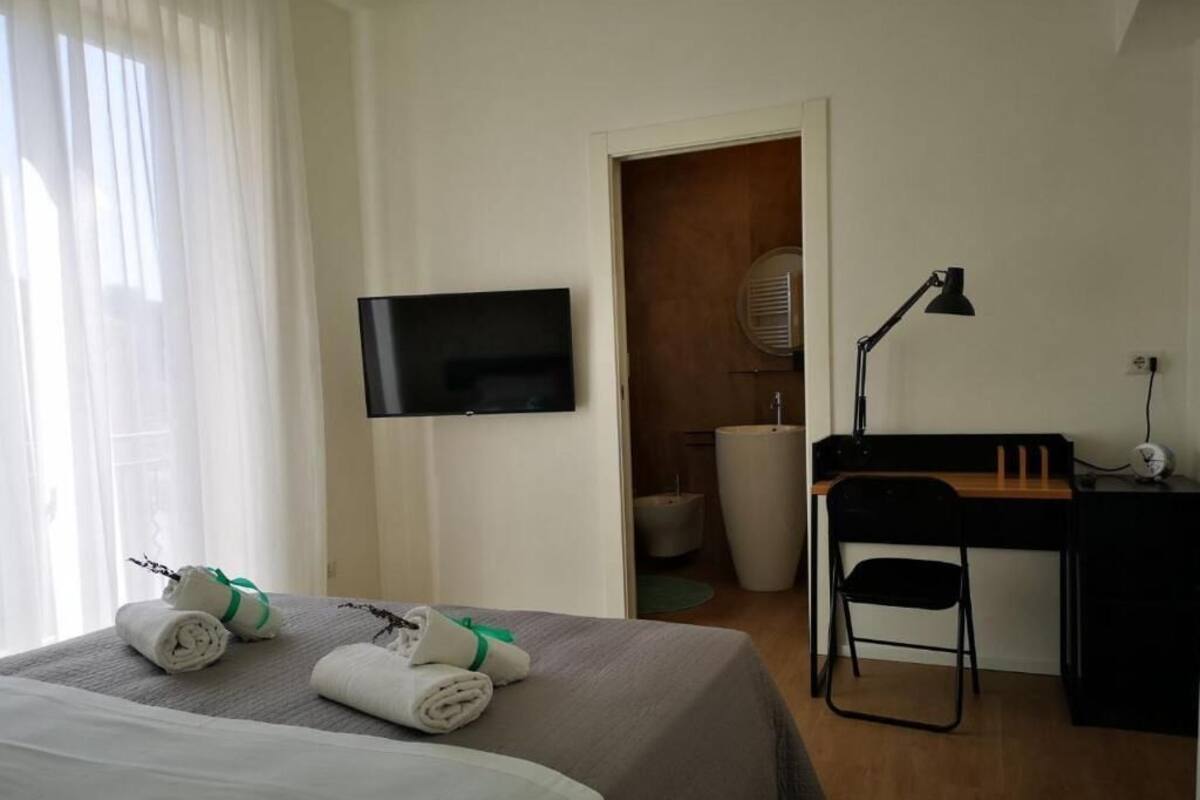 Quarto de hotel com duas camas, uma escrivaninha, uma cadeira, uma televisão e um banheiro visível por uma porta aberta.