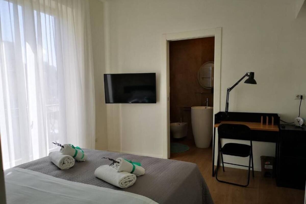 Quarto de hotel com uma cama, uma mesa, uma cadeira, uma televisão e um banheiro visível por uma porta aberta.