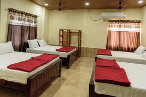 Quarto de hotel com quatro camas, cada uma com um cobertor vermelho, cabeceiras de madeira e um ventilador de teto.