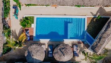 Vista aérea de uma piscina retangular com um deck ao redor, cadeiras de espreguiçadeira e guarda-sóis de palha.