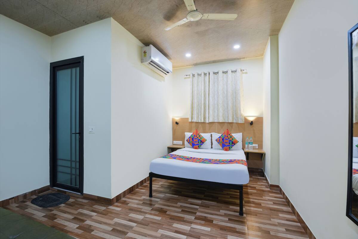 Quarto com cama, ventilador de teto, ar condicionado, mesa de cabeceira e janela com cortinas.