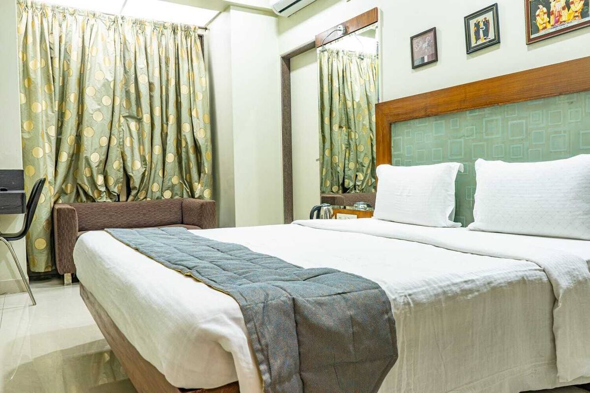 Quarto de hotel com cama, cadeira, mesa de cabeceira, espelho e cortinas.