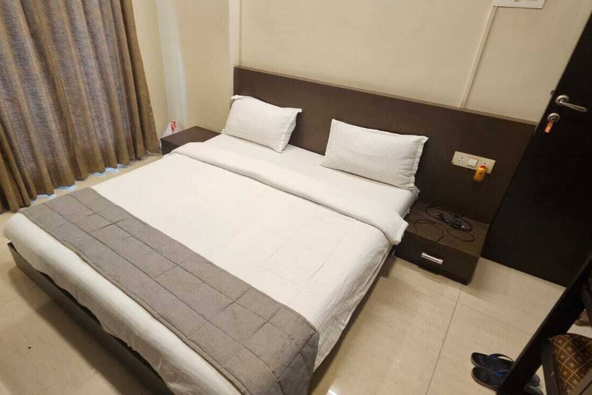 Quarto de hotel com cama, mesa de cabeceira, porta e cortina.