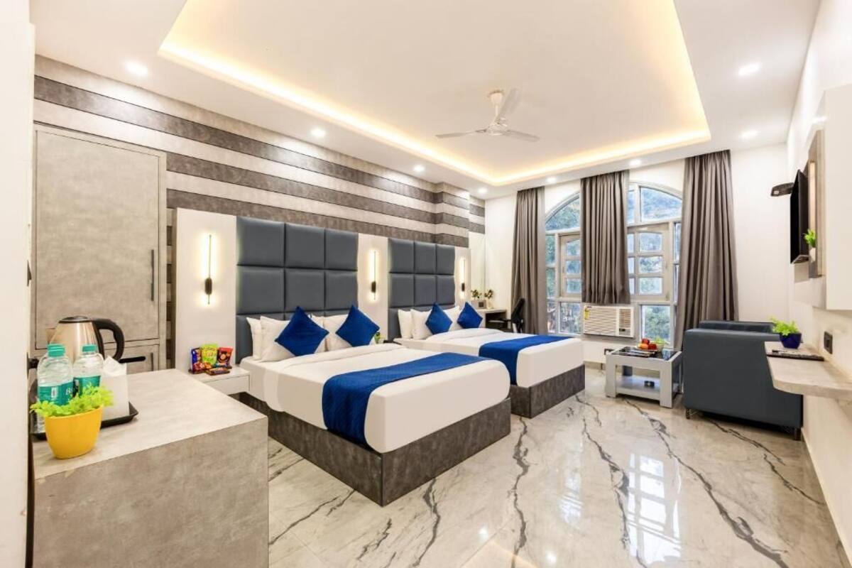 Quarto de hotel com duas camas, uma escrivaninha, uma cadeira, uma televisão e uma janela com cortinas.