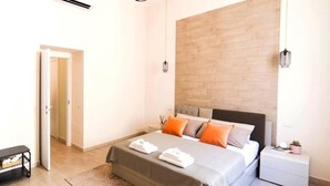 Quarto com cama, almofadas, mesa de cabeceira, luminária e porta.