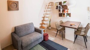 Uma sala de estar moderna com um sofá, uma mesa de jantar com cadeiras, uma escada e uma estante de livros.