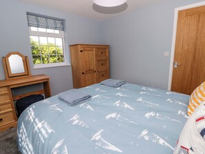 Quarto com cama, cômoda de madeira, escrivaninha com espelho e janela com vista para o verde.