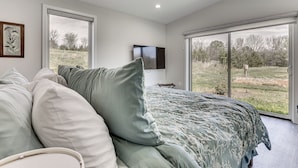 Quarto com cama, travesseiros, televisão e amplas janelas com vista para o exterior.