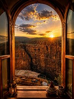 Vista pela janela de uma paisagem montanhosa ao pôr do sol, com uma pequena área de estar ao ar livre visível abaixo.