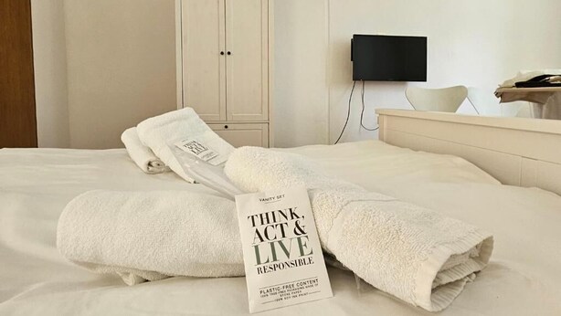 Quarto de hotel com cama, televisão, guarda-roupa e toalha com uma mensagem.