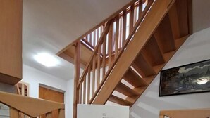 Uma escada de madeira leva a um andar superior, uma mesa branca com um livro e um quadro na parede.