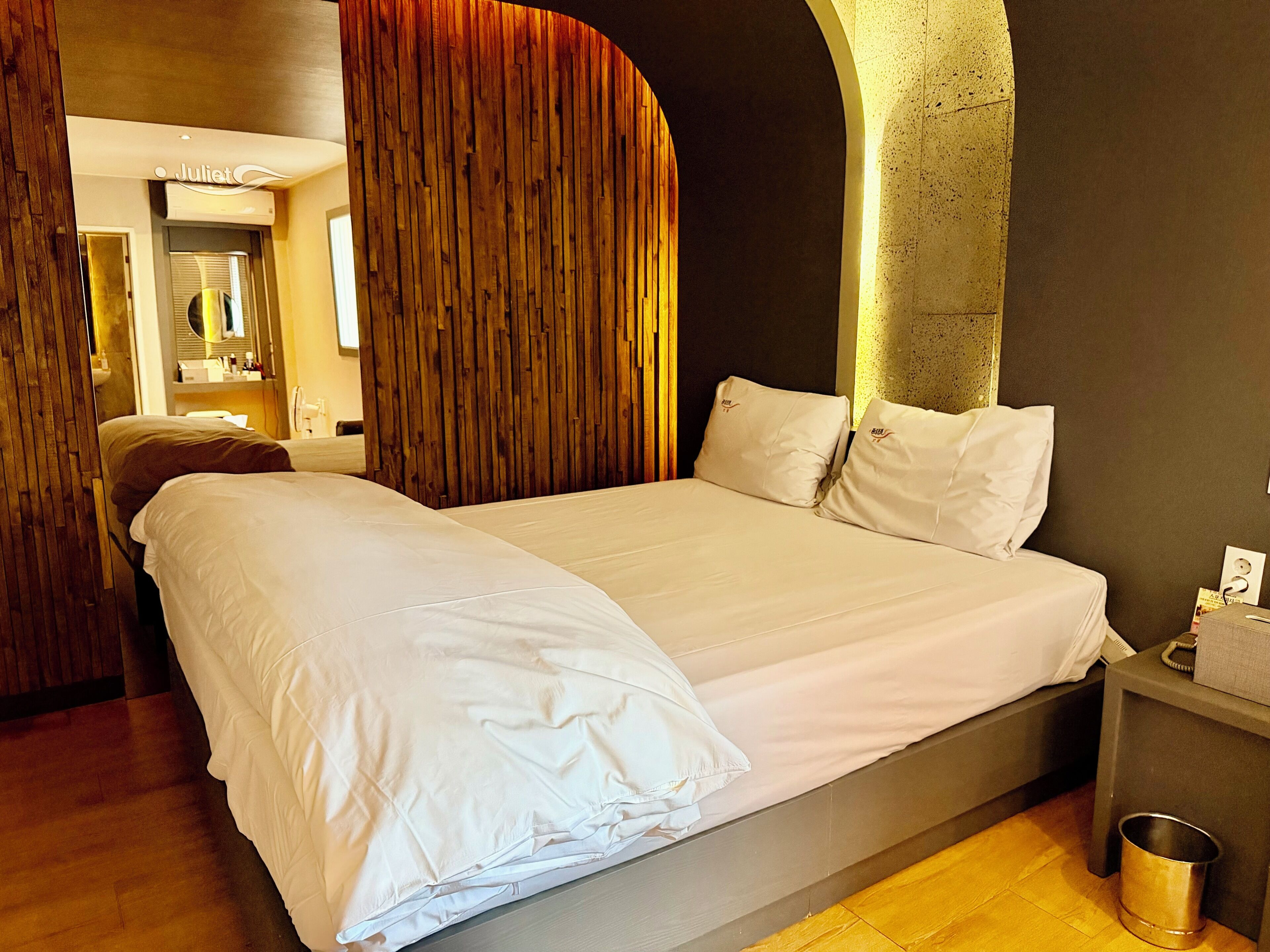 Quarto de hotel com uma cama grande, parede de painel de madeira e banheiro visível com um espelho.