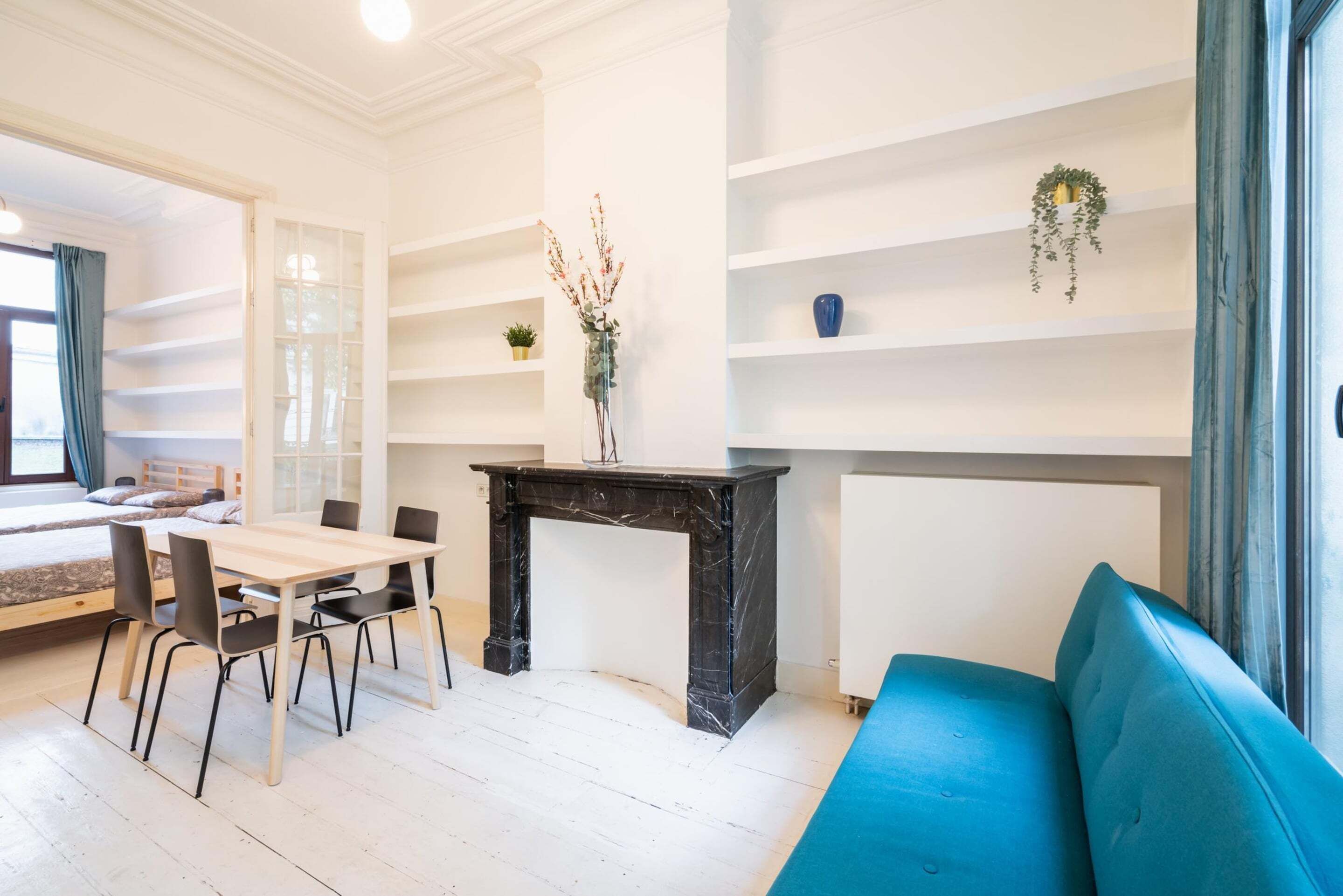 Um quarto com cama, uma mesa de jantar com cadeiras, um sofá azul, lareira e estantes com plantas.