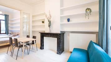 Um quarto com cama, uma mesa de jantar com cadeiras, um sofá azul, lareira e estantes com plantas.