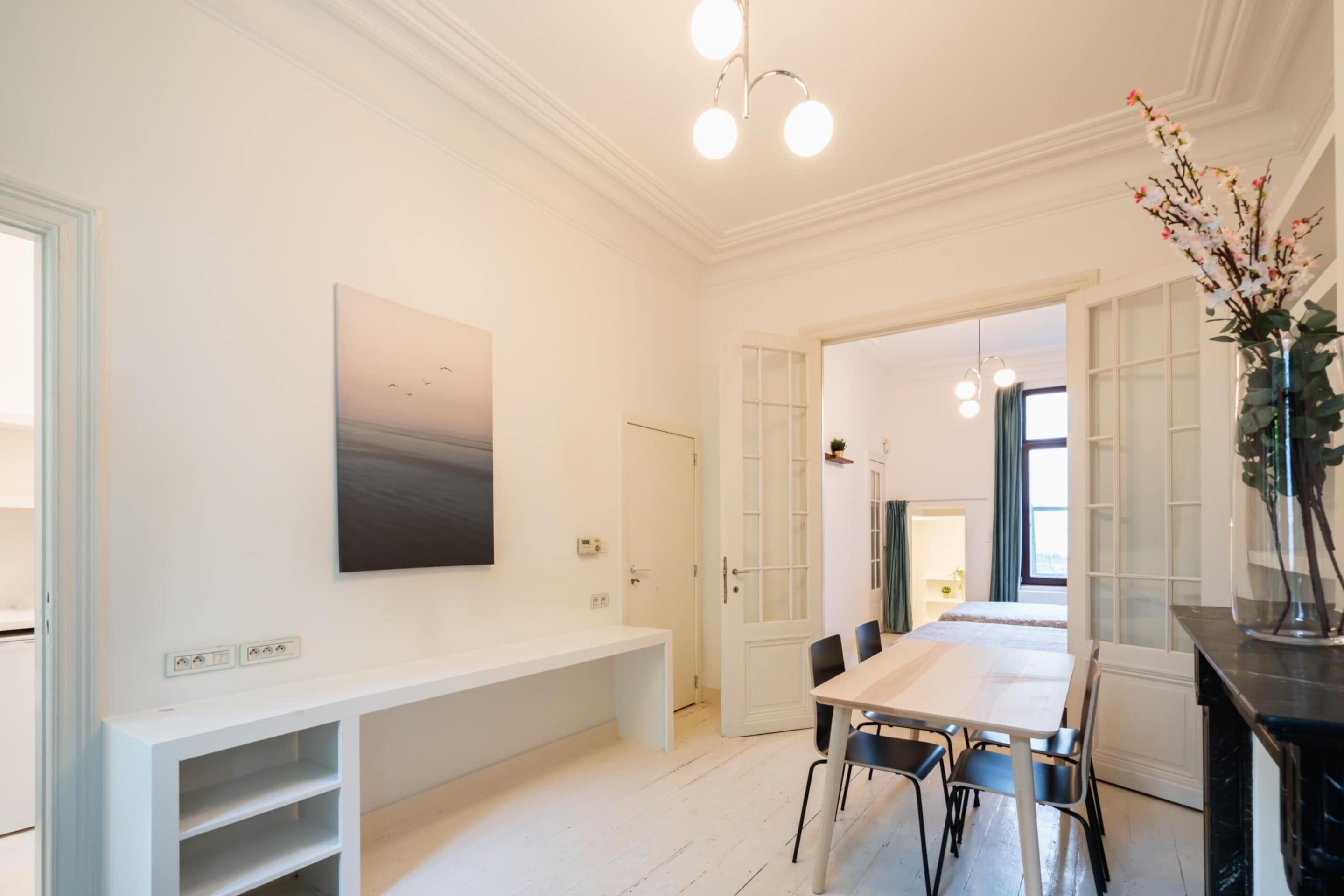 Um interior moderno com um banco branco, uma mesa de jantar com cadeiras, um quadro e um vaso com flores.