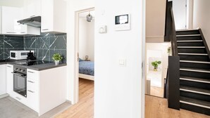 Cozinha moderna com armários brancos, micro-ondas e máquina de café. Piso de madeira e escada que dá para outro cômodo.