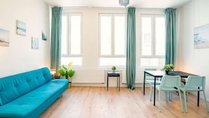 Quarto com sofá verde-água, uma mesa de jantar com cadeiras, uma mesinha lateral e um radiador.