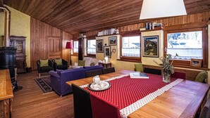 Um quarto acolhedor com paredes e teto de madeira, uma mesa de jantar com toalha vermelha, um sofá e uma lareira.