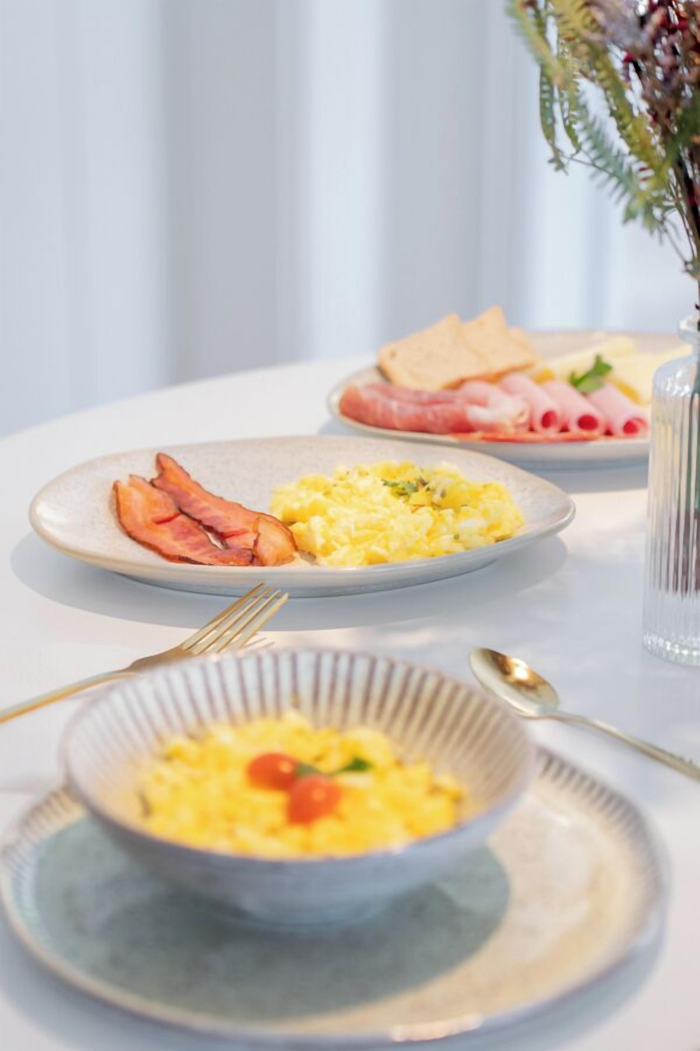 Uma mesa de café da manhã com ovos, bacon e torradas, e uma tigela de frutas.
