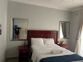 Quarto de hotel com cabeceira de madeira, um espelho grande, mesa de cabeceira com abajur e janela com cortinas.