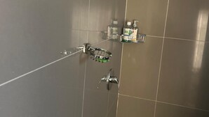 Área de chuveiro com chuveiro manual, torneira fixada na parede e dosador de sabonete.