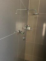 Área de chuveiro com chuveiro manual, torneira fixada na parede e dosador de sabonete.