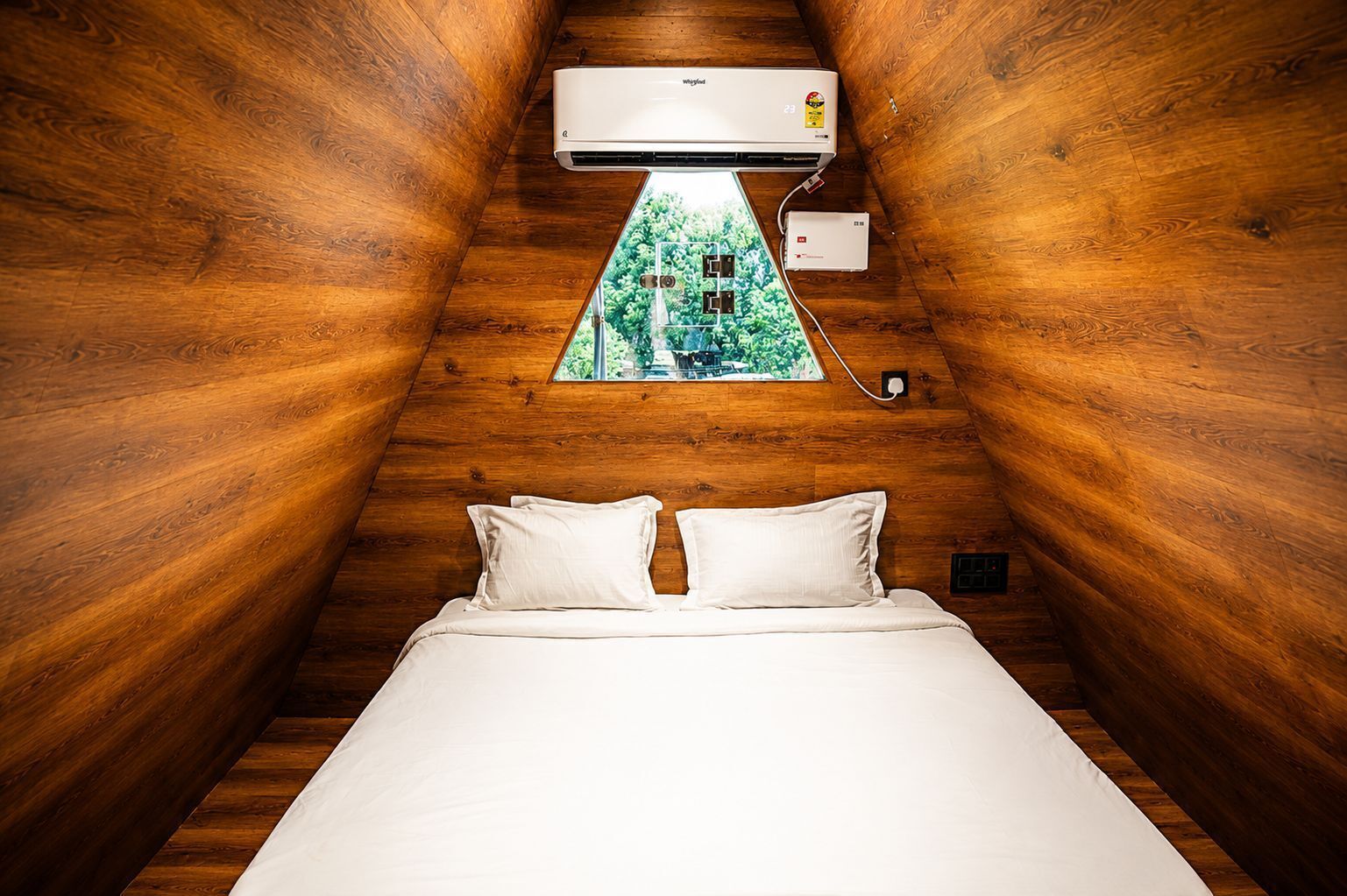 Quarto com cama, paredes de madeira, janela com vista e aparelho de ar condicionado.