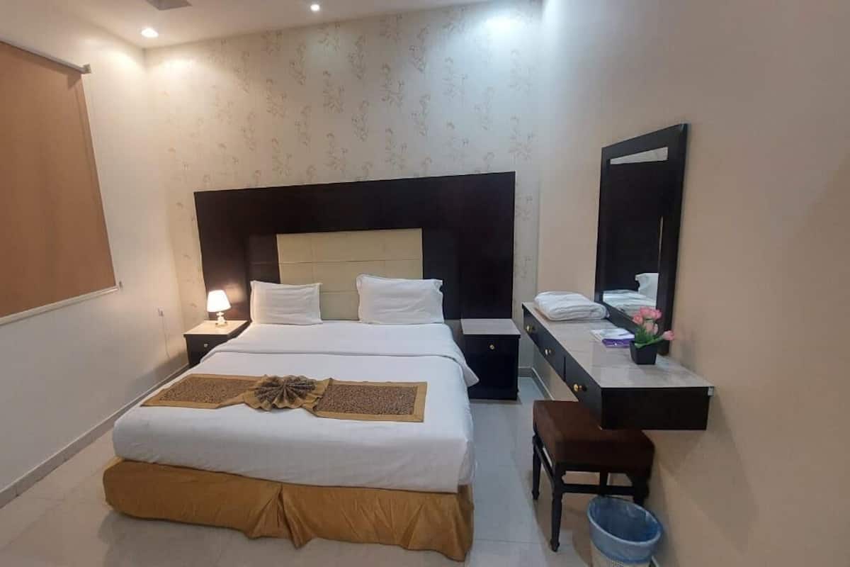 Quarto de hotel com cama, mesa de cabeceira, cadeira, escrivaninha e espelho.