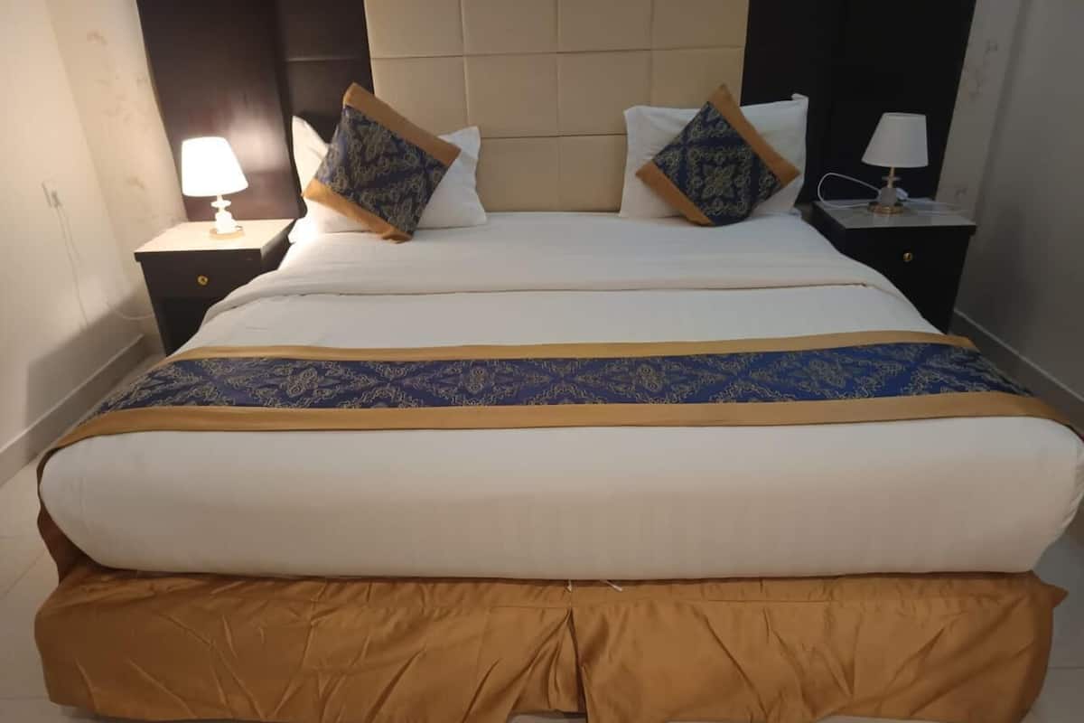 Uma cama com cabeceira, duas mesas de cabeceira com abajures e um cobreleito estampado.