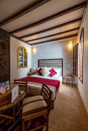 Quarto com cama, cabeceira de madeira e uma pequena mesa com cadeiras.