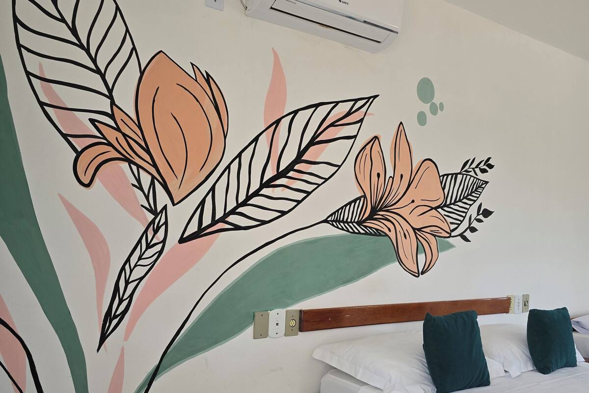 Quarto de hotel com uma cama, ar condicionado fixado na parede e um mural floral.