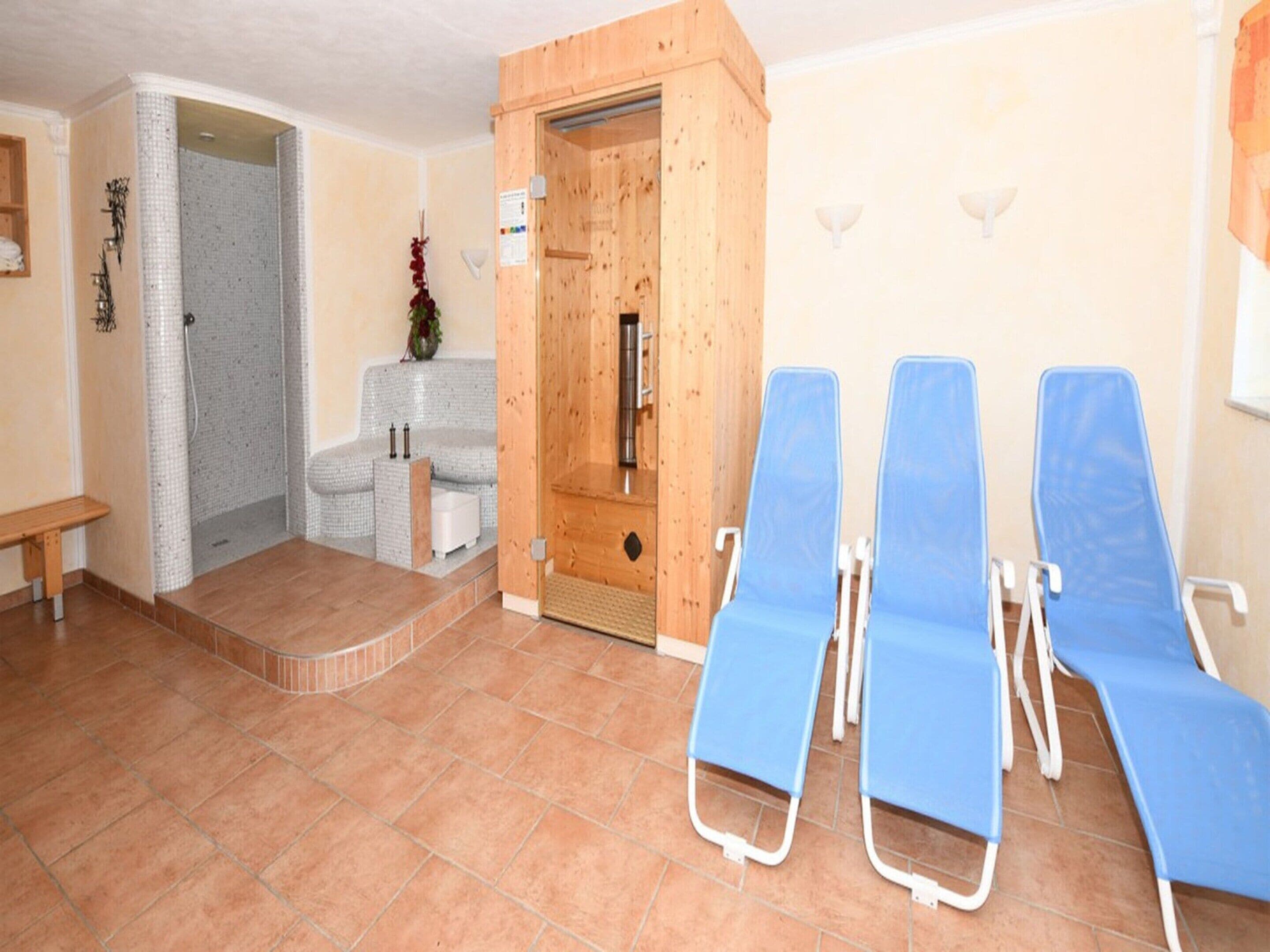 Uma sala de sauna com porta de madeira, um banco e três cadeiras reclináveis azuis.