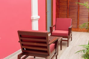 Um conjunto de banco e cadeira de madeira em frente a uma parede rosa, com uma porta de madeira e uma planta de bambu ao fundo.
