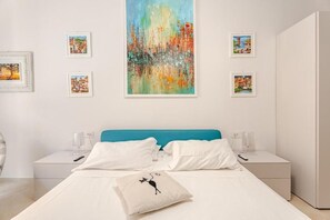 Quarto moderno com cama, duas mesas de cabeceira, um criado-mudo e uma grande pintura abstrata na parede.