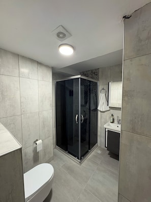 Casa de banho moderna com cabine de duche de vidro, lavatório branco e sanita.