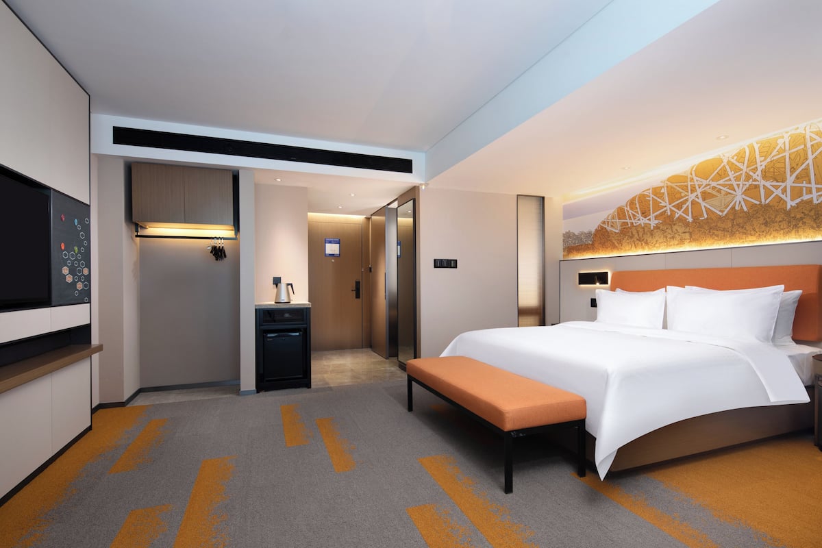 Quarto de hotel moderno com uma cama grande, um banco, uma TV, uma mesa de escritório e um banheiro.