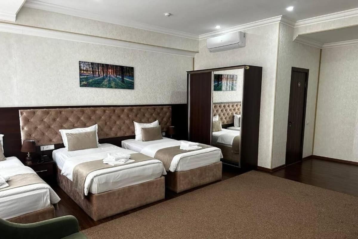 Quarto de hotel com duas camas, um espelho grande, uma poltrona verde e um quadro na parede.
