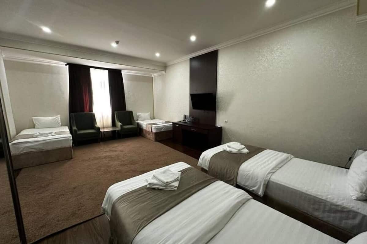 Quarto de hotel com duas camas, uma escrivaninha, uma cadeira, uma televisão e uma janela com cortinas.
