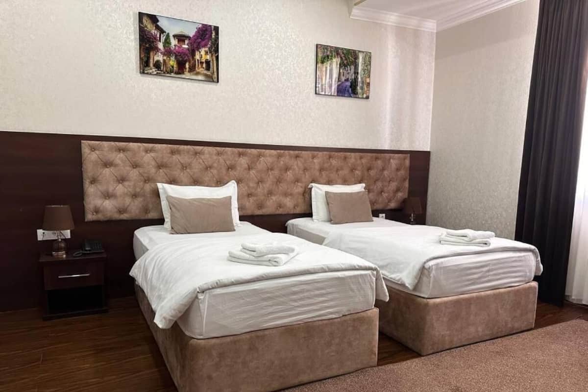 Quarto de hotel com duas camas, uma cabeceira grande, uma mesa de cabeceira e duas obras de arte penduradas na parede.