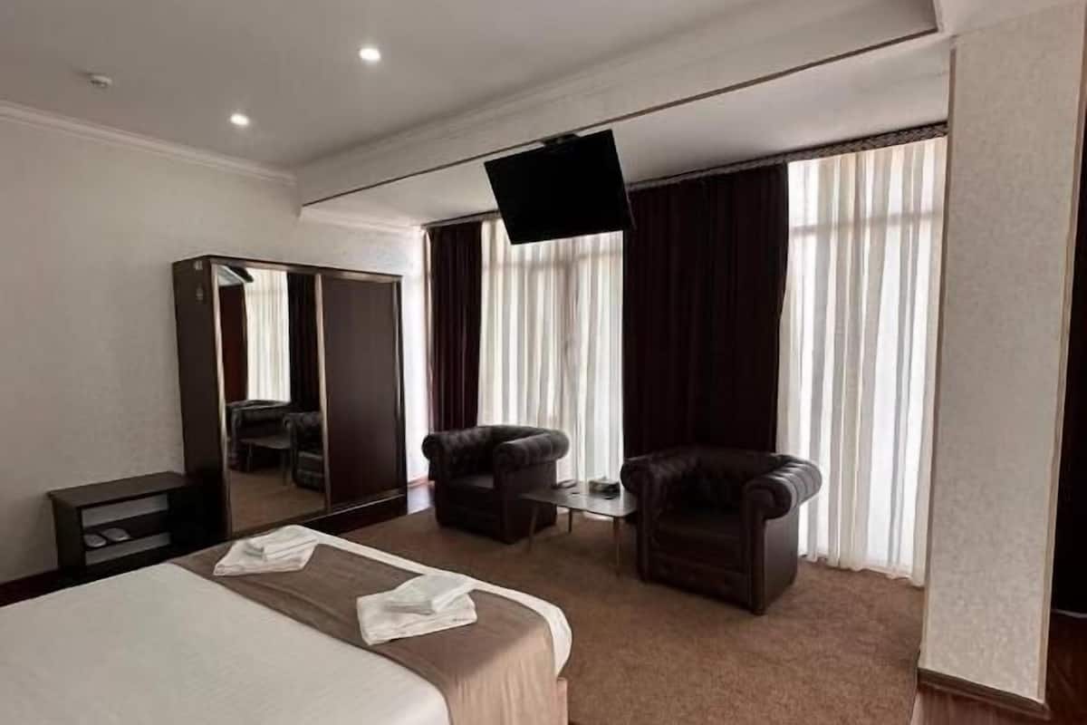 Quarto de hotel com cama, escrivaninha, cadeira, televisão e uma grande janela com cortinas.